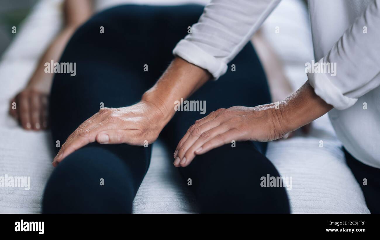 Female Reiki practitioner healing a patient's knees chakras Stock Photo ...