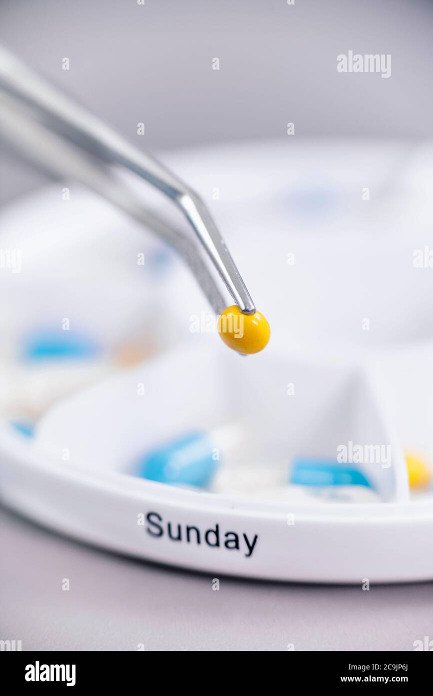 Sorting medications. Hands sorting medication with tweezers into 7 day ...