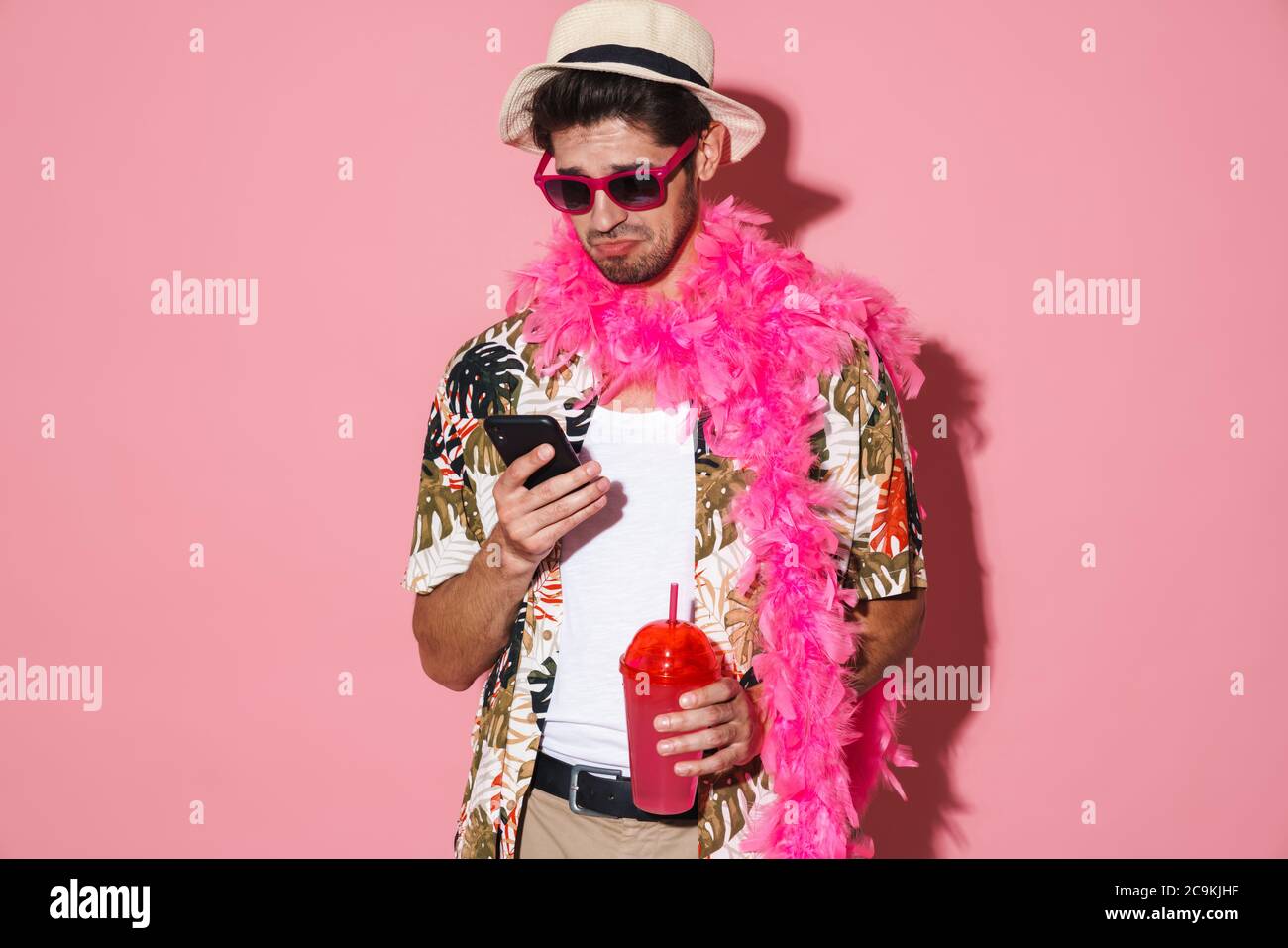 Portrait of unhappy man wearing boa using cellphone while drinking soda ...
