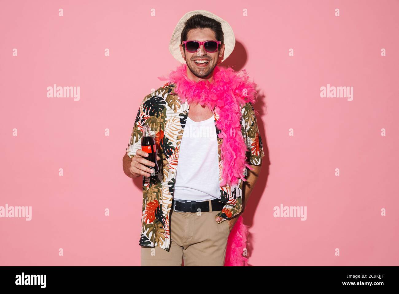 Portrait of cheerful young man wearing boa laughing while drinking soda ...
