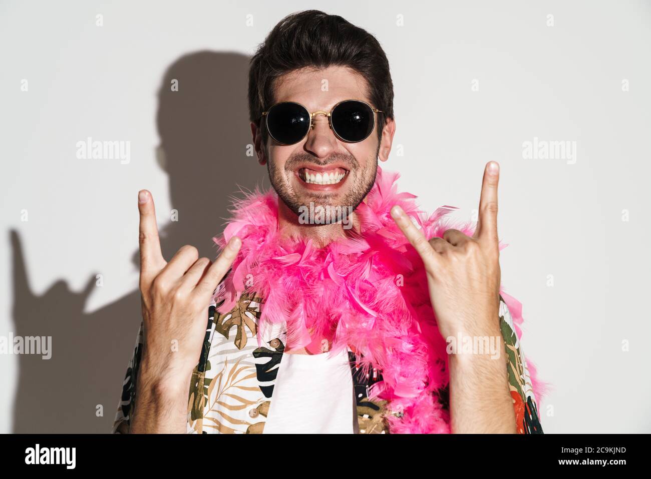 Portrait of handsome excited man wearing boa making horns gesture with ...