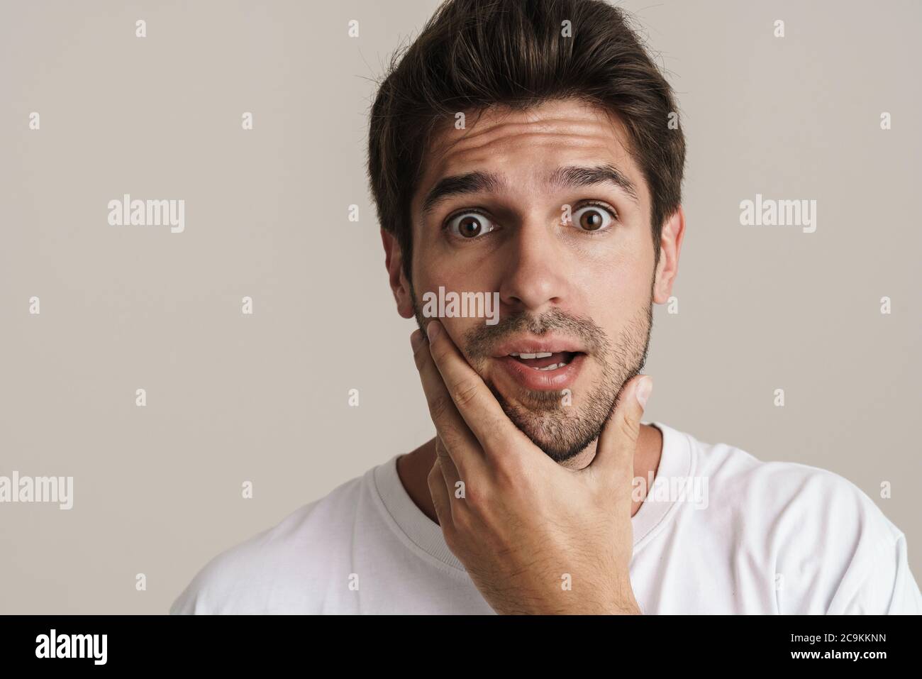 Portrait of shocked young man in basic t-shirt expressing surprise on ...