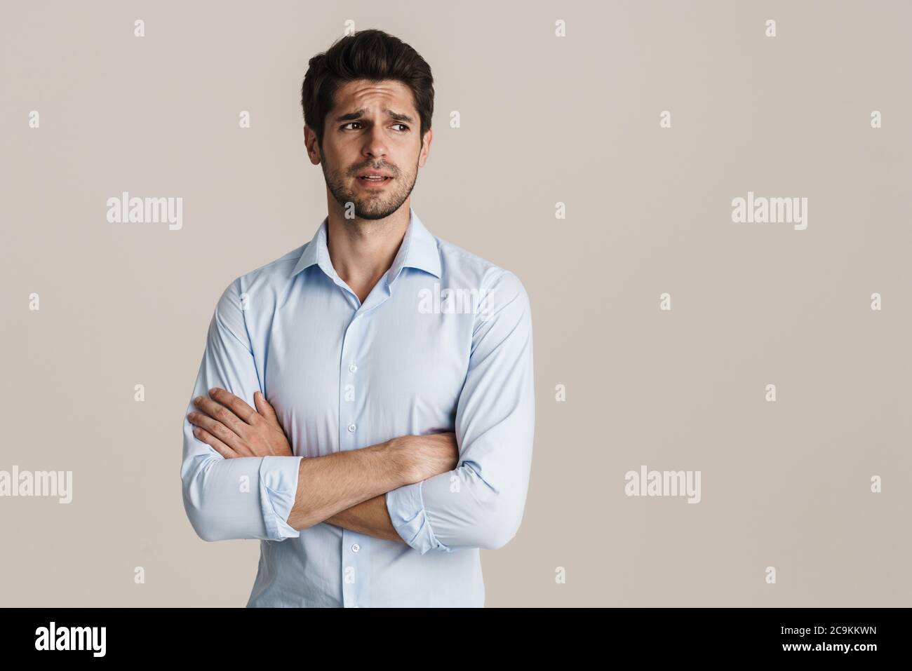 Portrait of sad handsome man looking aside while posing with arms ...
