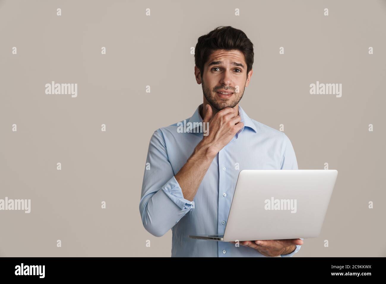 Portrait of confused handsome man looking at camera while using ...