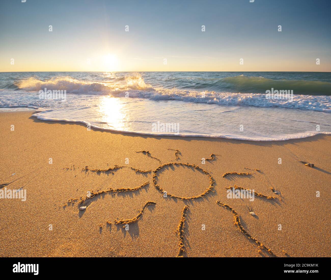 Sun drawing drawn on a beach on the golden sea sand. Wave and foam on ...
