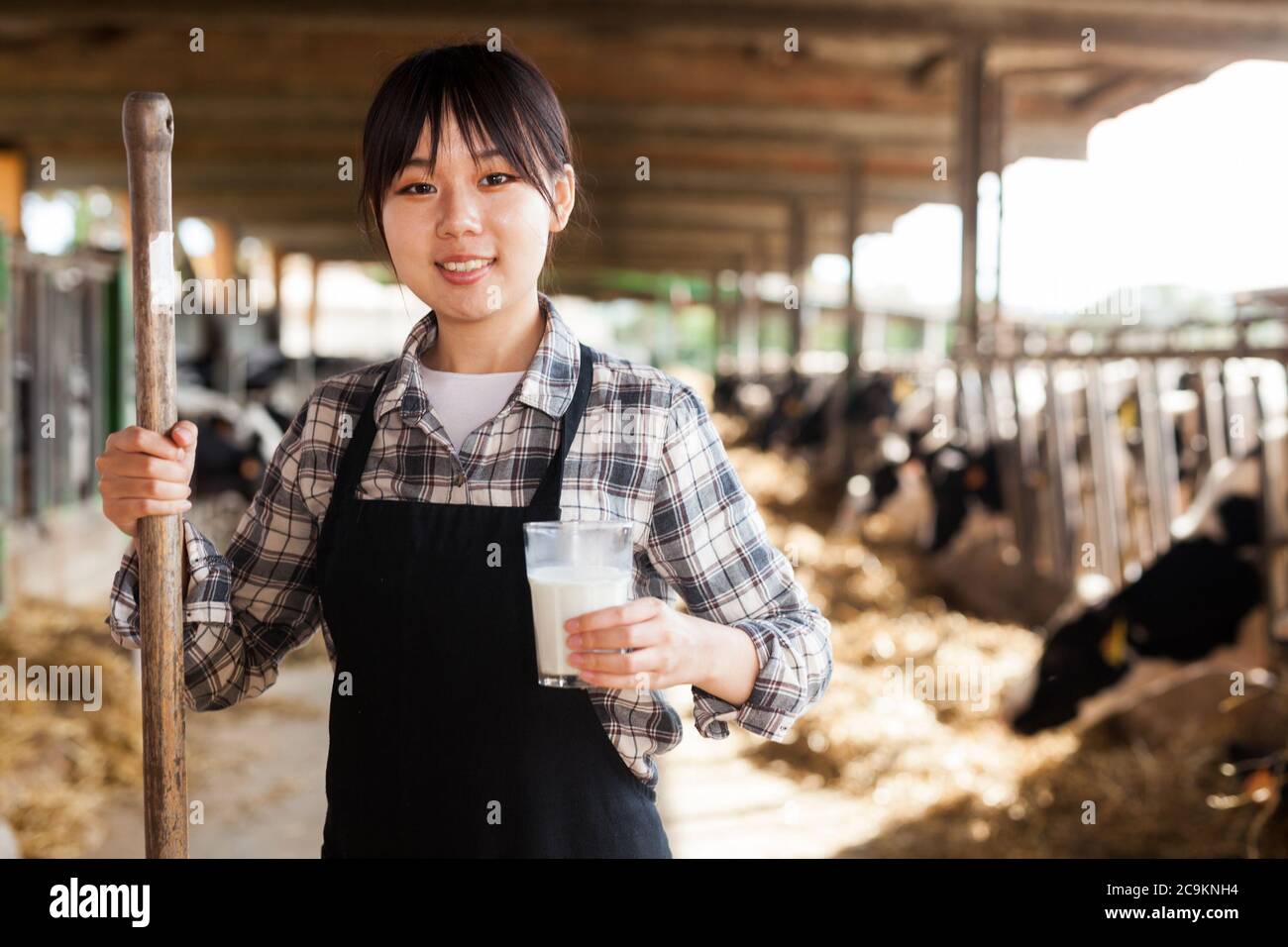 Young positive female dairy farm worker standing with glass of fresh ...