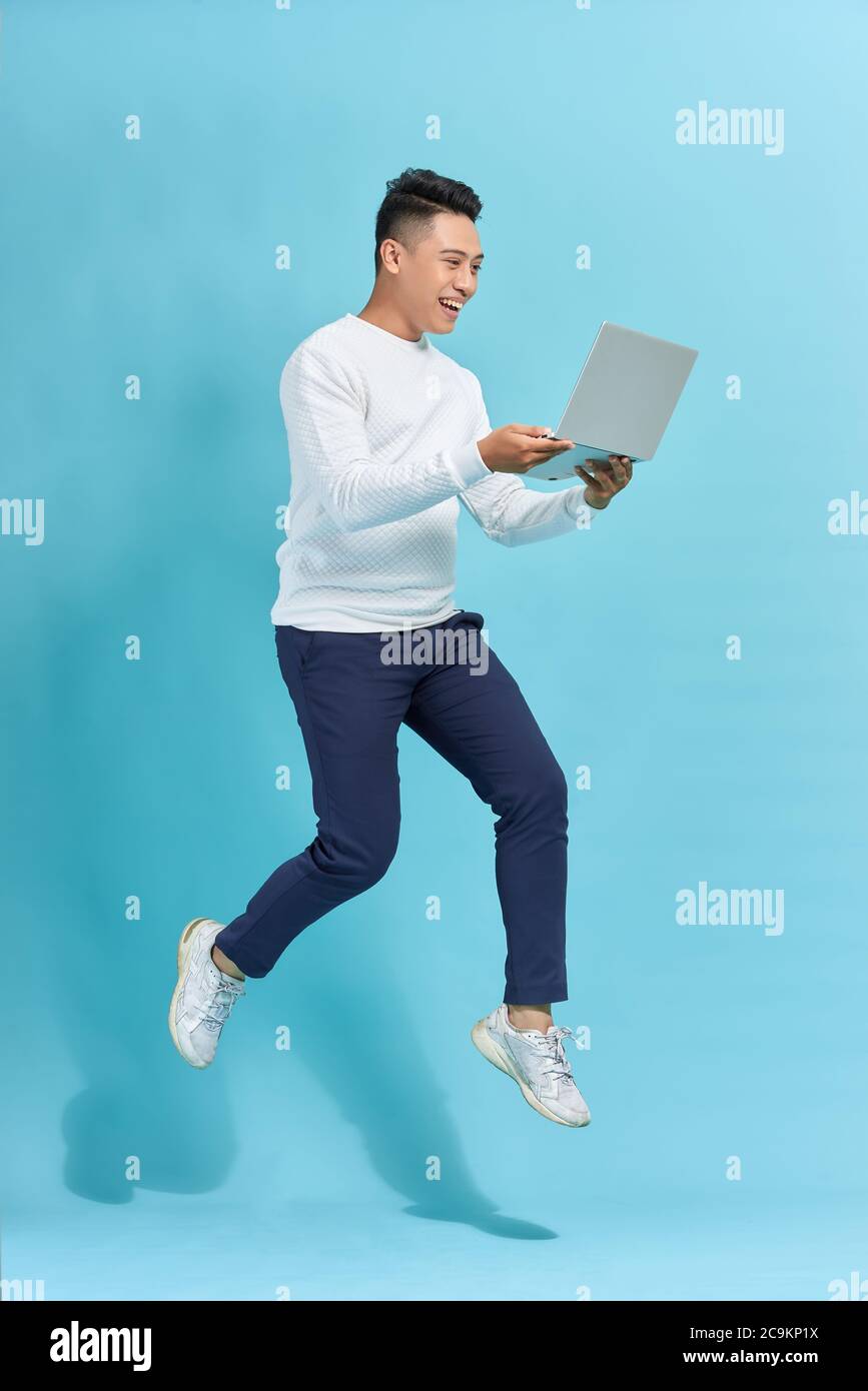 Full length portrait of happy man jumping and holding laptop isolated ...