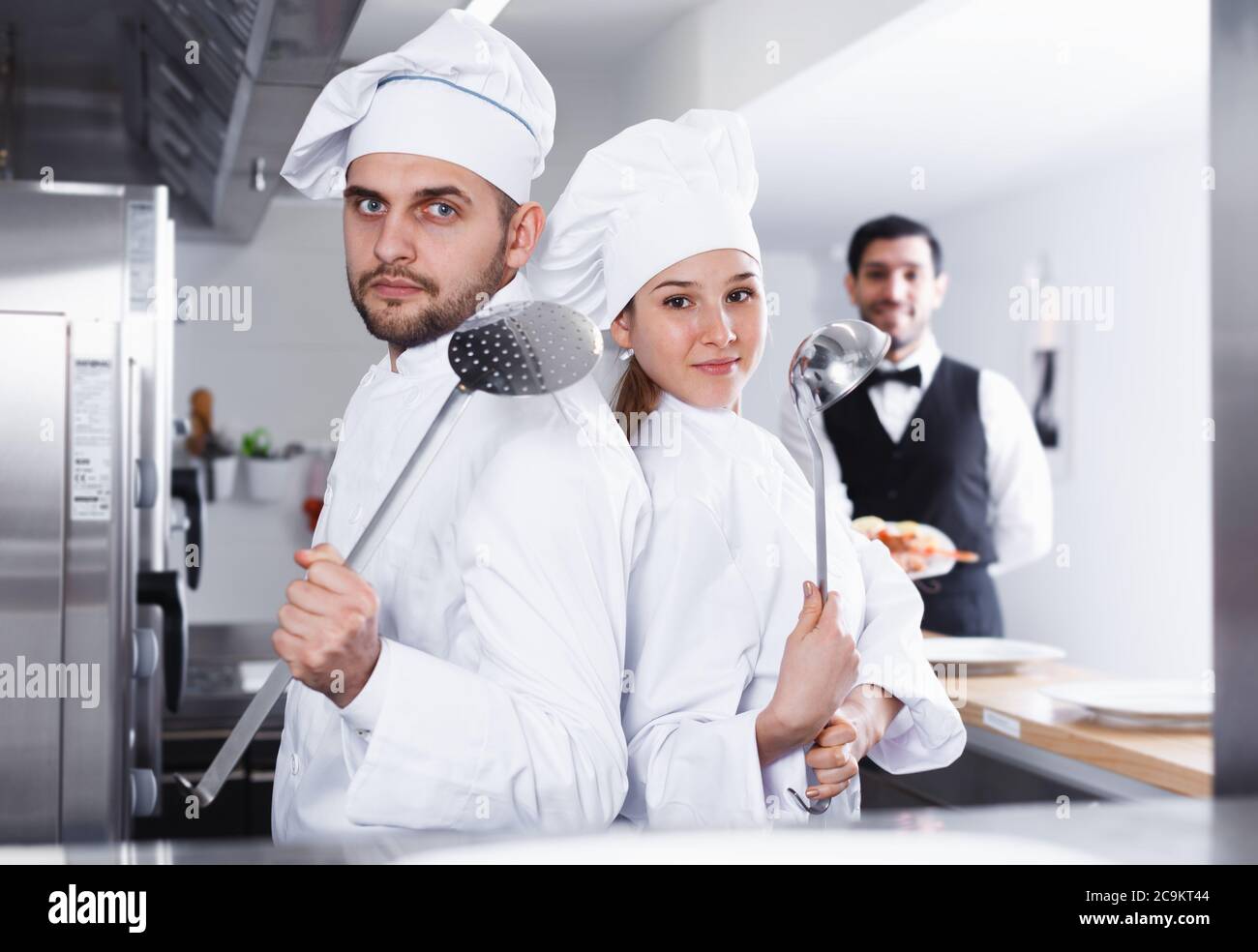 Portrait of two professional cooks in kitchen, restaurant waiter with ...