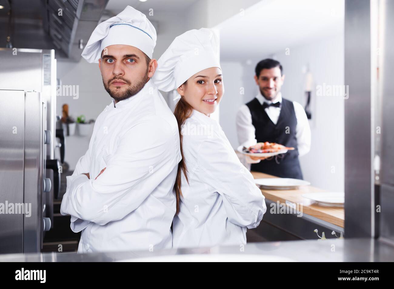two confident fish restaurant chefs, standing back to back in kitchen ...