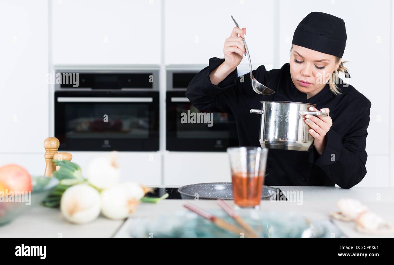 Smiling woman kitchener in uniform is salt soup in pot in the kitchen ...