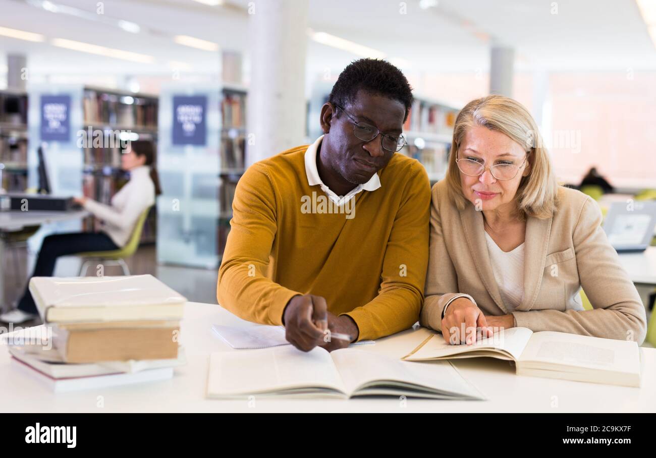 Two adult students studying together in public library Stock Photo - Alamy