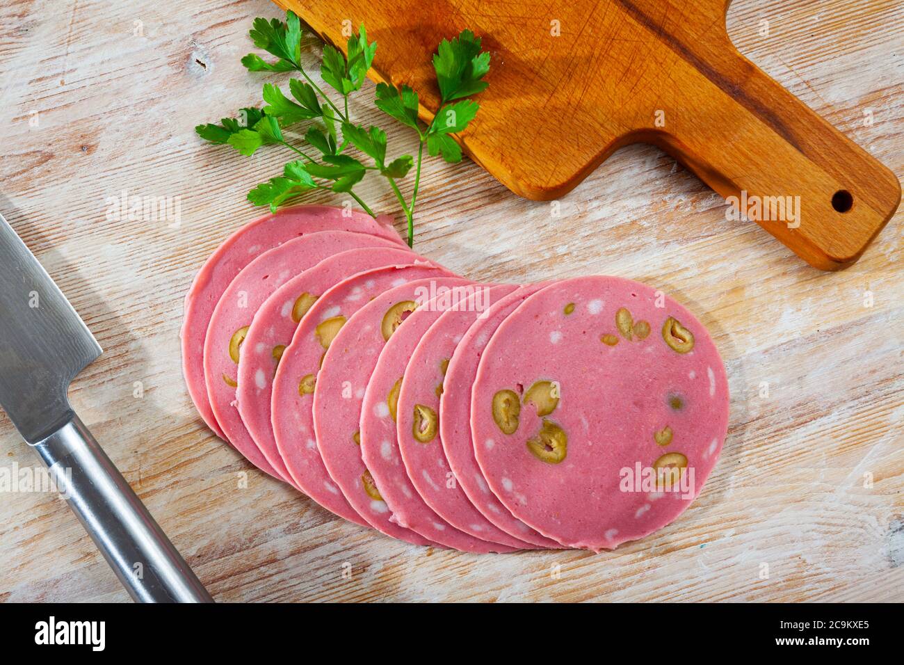 Thin sliced Spanish Mortadella sausage with olives on wooden background ...