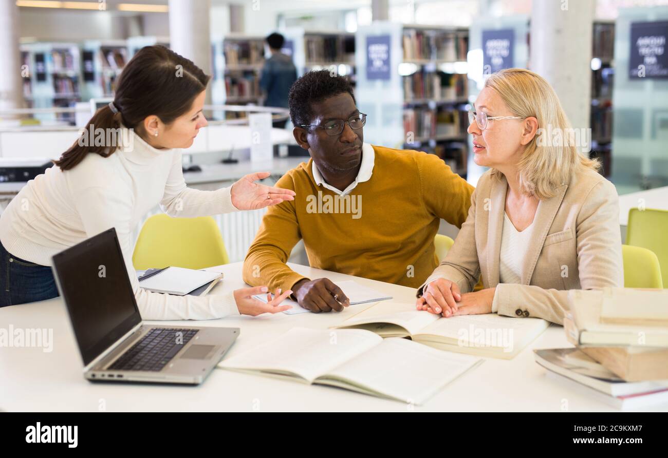Female tutor helping students preparing for exam in library Stock Photo ...
