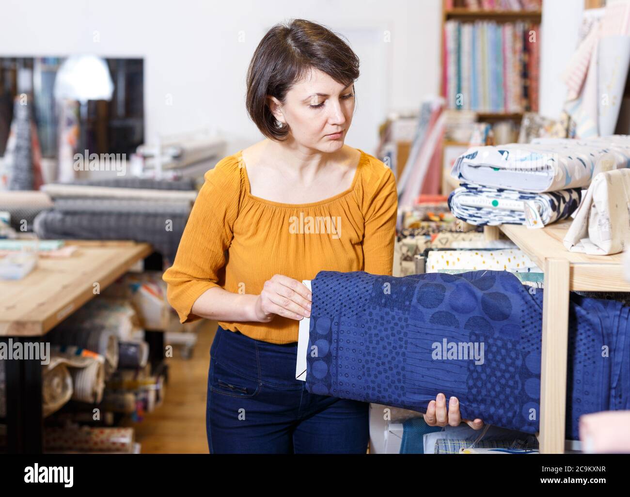 Female seller organizing assortment of textile on shelves in fabric ...