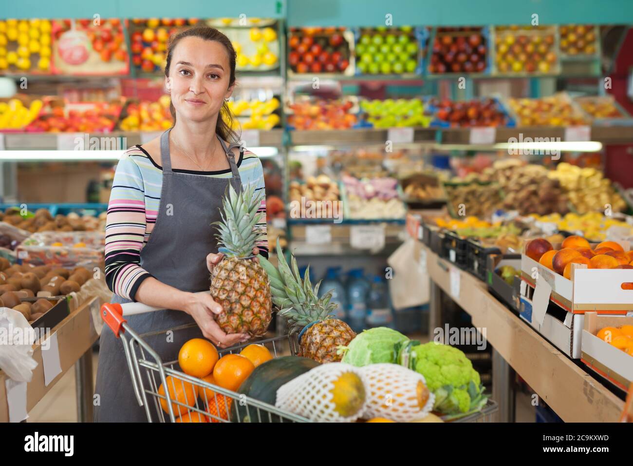 Modern woman store worker in apron at fruit department of supermarket ...