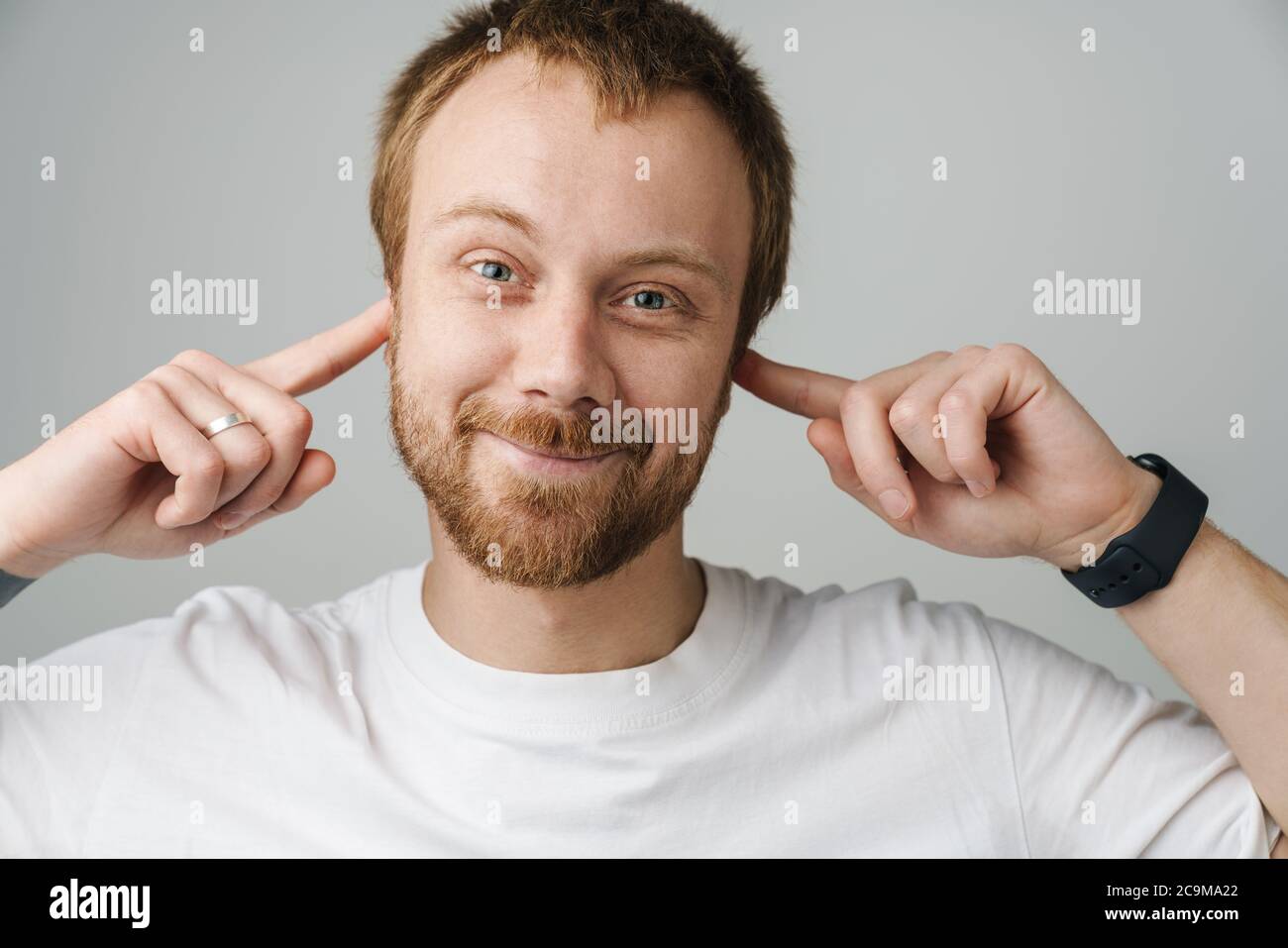 Photo of joyful young man with red hair plugging his ears and smiling ...