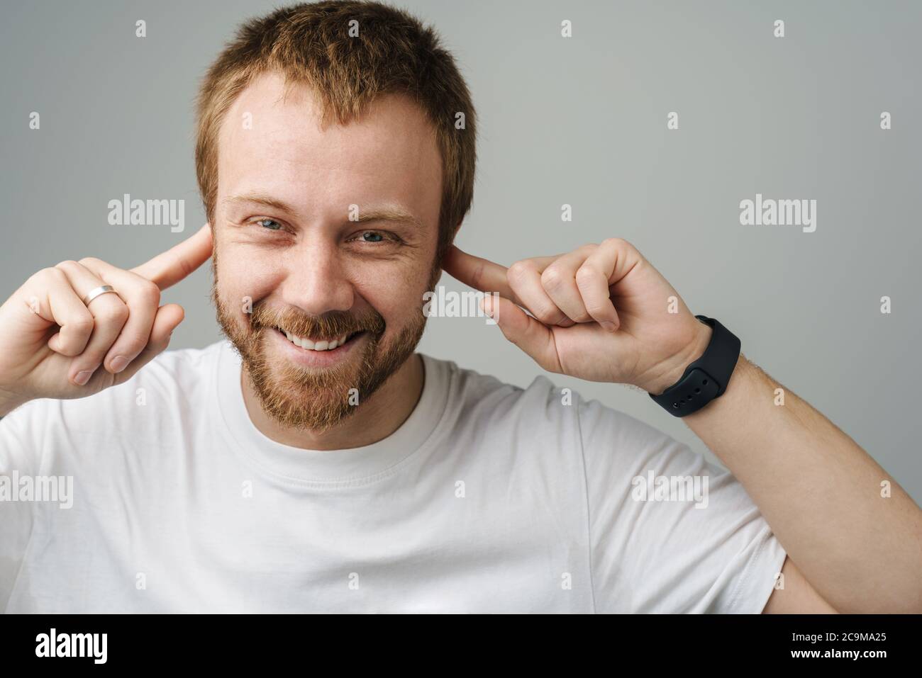Photo of joyful young man with red hair plugging his ears and smiling ...