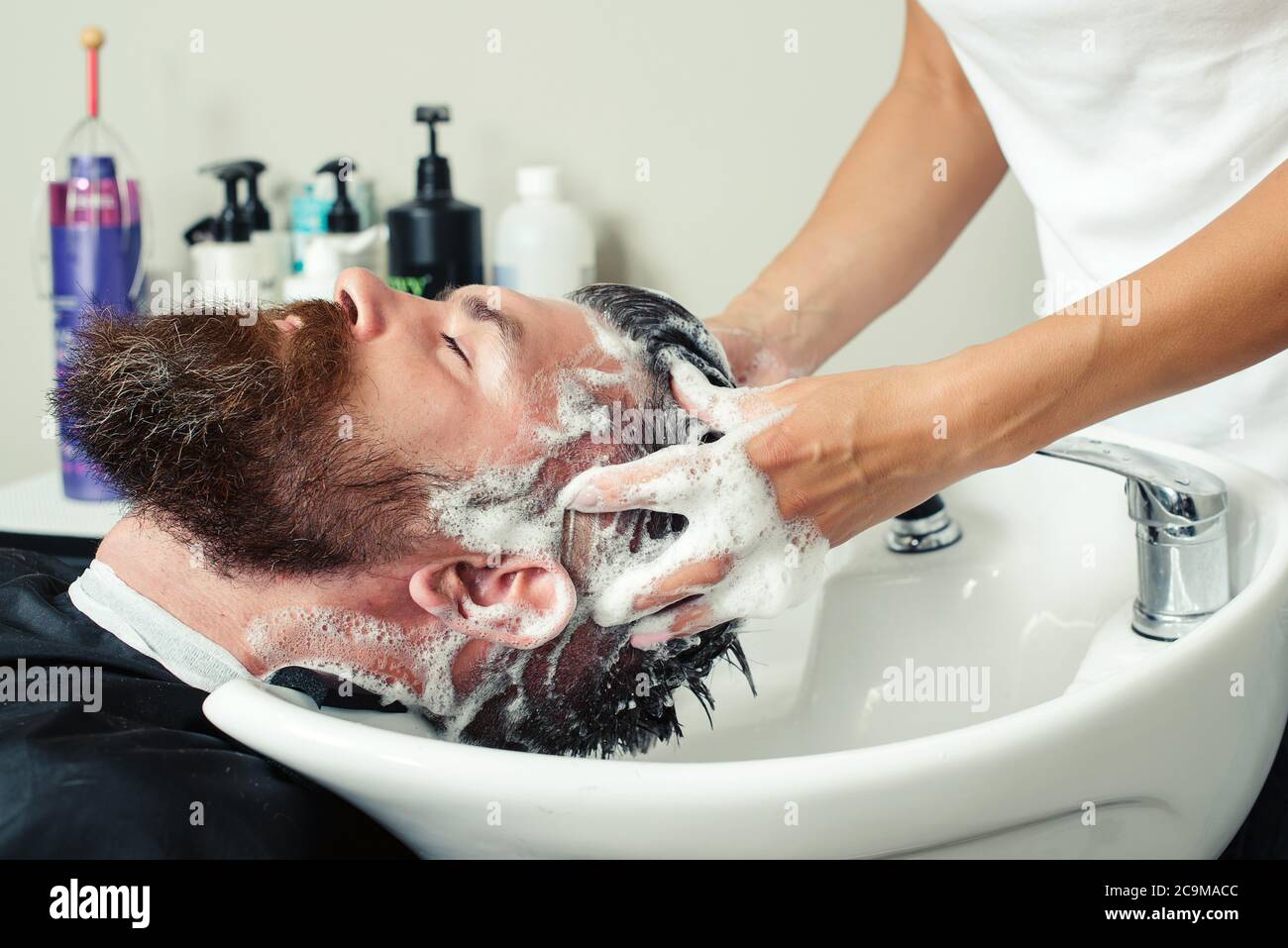 Close-up of brutal caucasian man having his hair washed in hairdressing ...