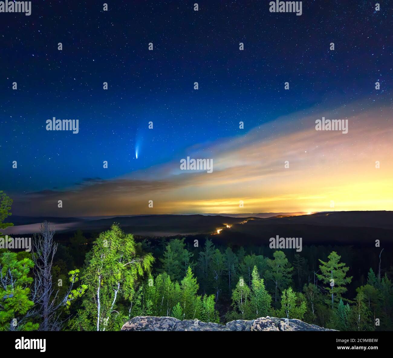 Neowise comet in the starry sky over the forest with city lights on the ...