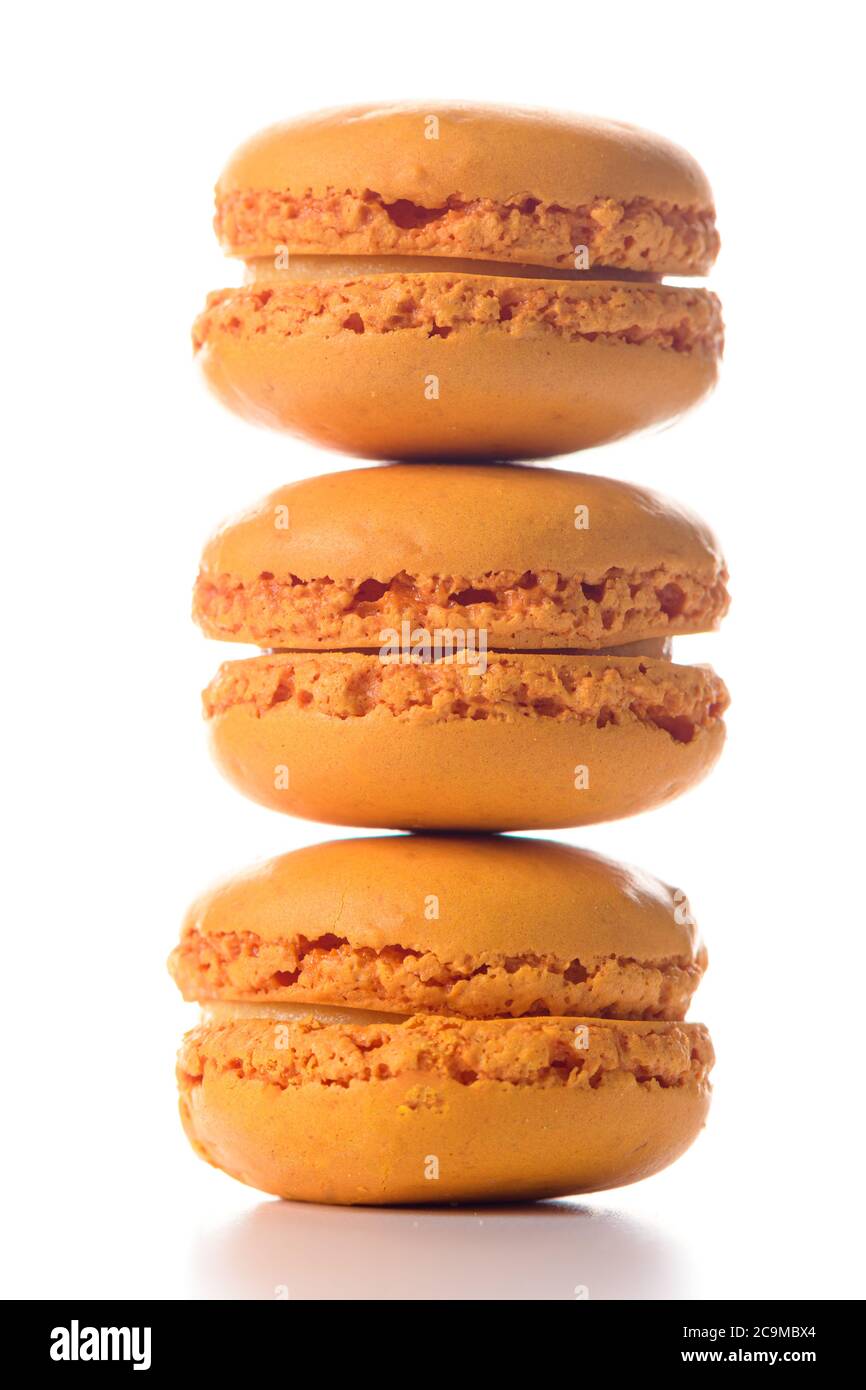 Three orange flavoured macaroons standing on top of each other on white ...