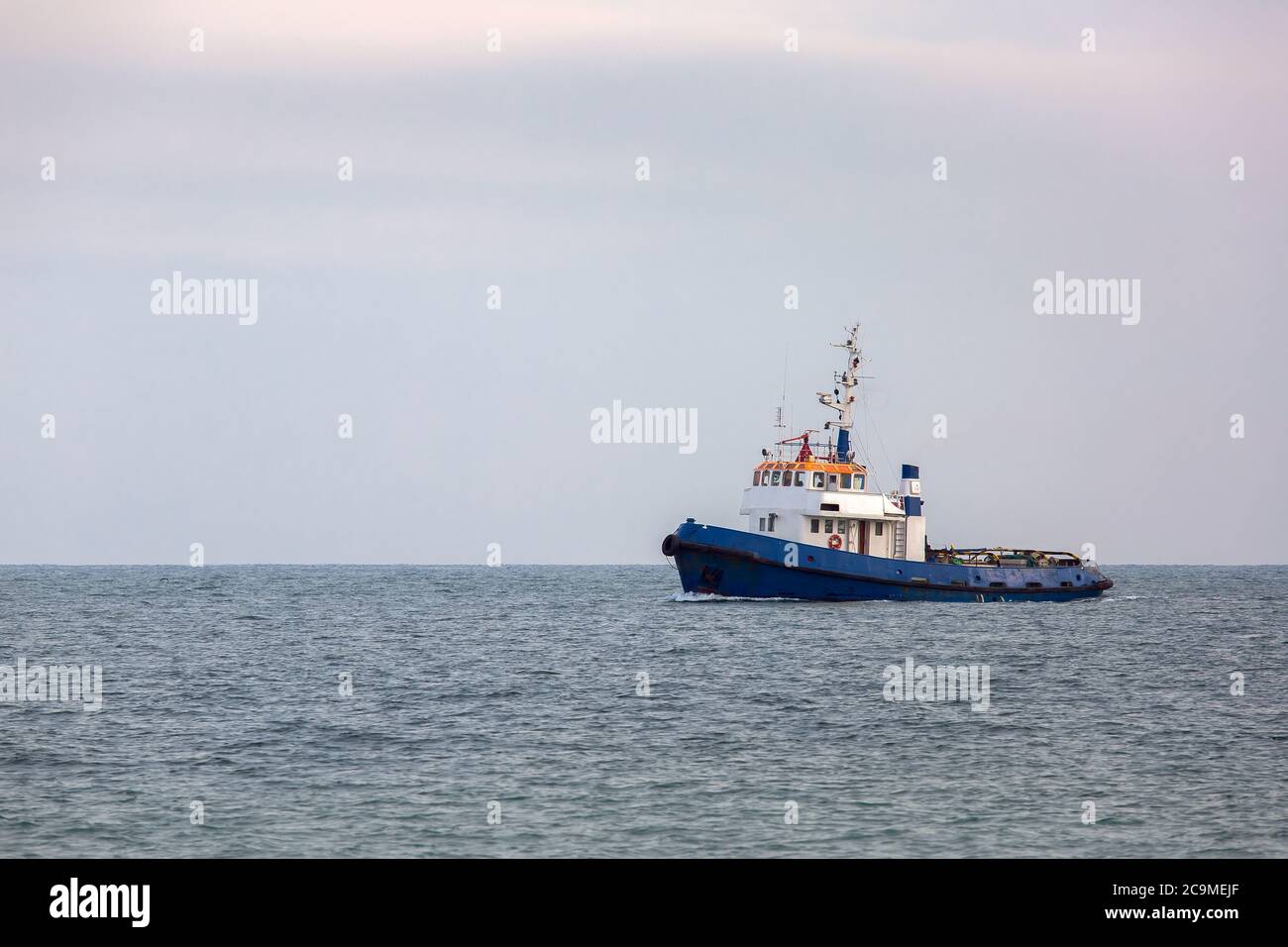 towing ship in the open sea, blue tugboat sailing on sea water against ...