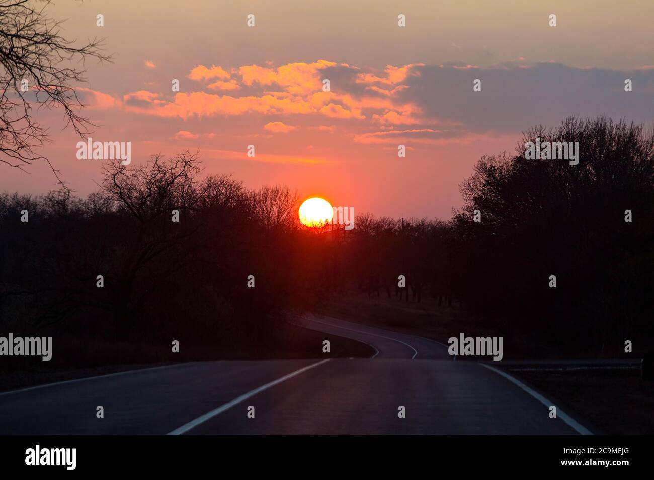 Sunny sunset on the horizon of a winding asphalt road with descents and ...