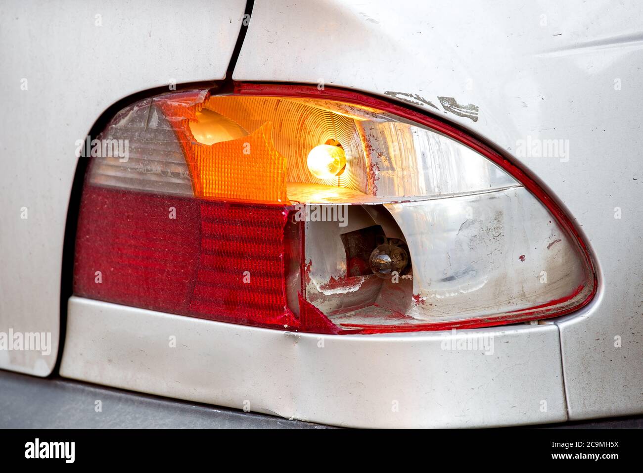 the broken tail lights of the gray car with the shining yellow lamp an ...