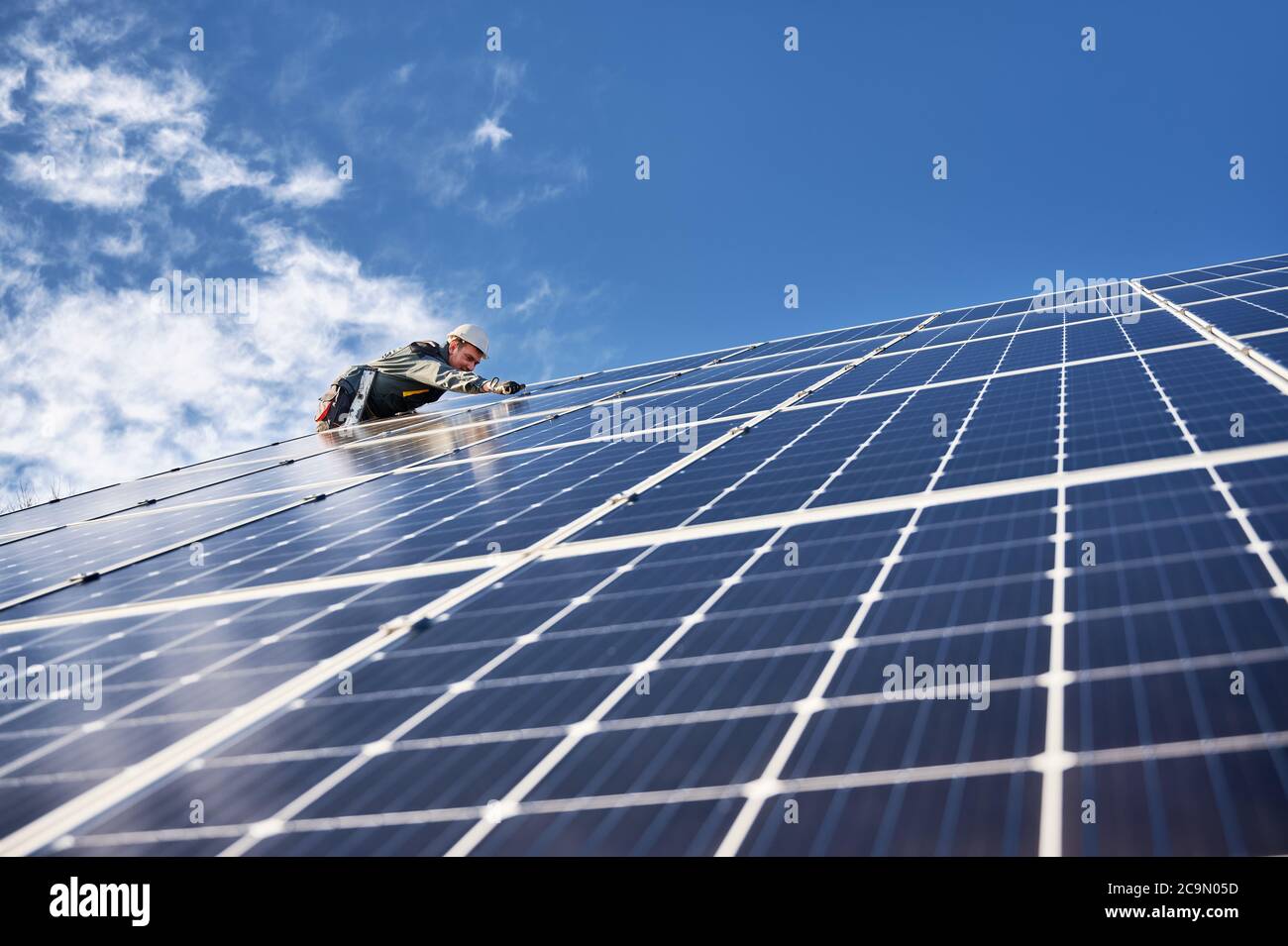 Male technician in safety helmet installing blue photovoltaic solar ...