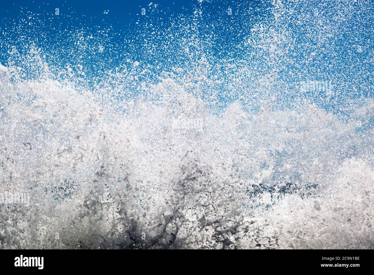 Spray from waves crashing over a rock, with a blue sky behind Stock ...