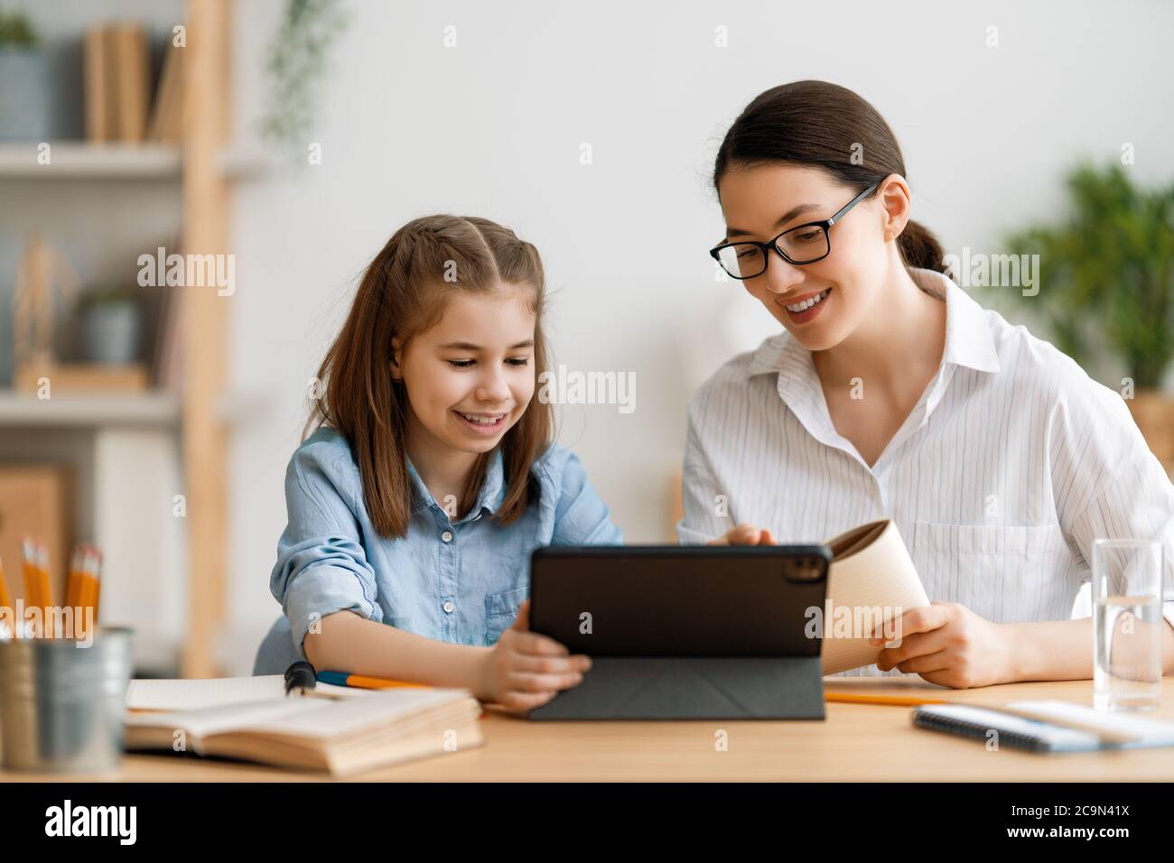 Back to school. Happy child and adult are sitting at desk. Girl doing ...