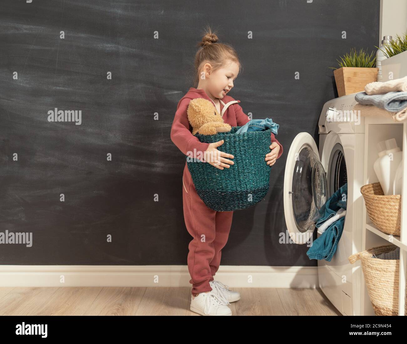 Child girl little helper is having fun and smiling while doing laundry ...