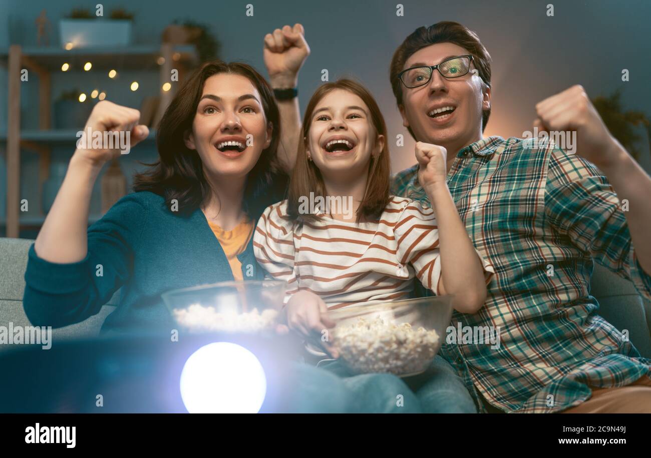 Happy family watching projector, TV, movies with popcorn in the evening ...