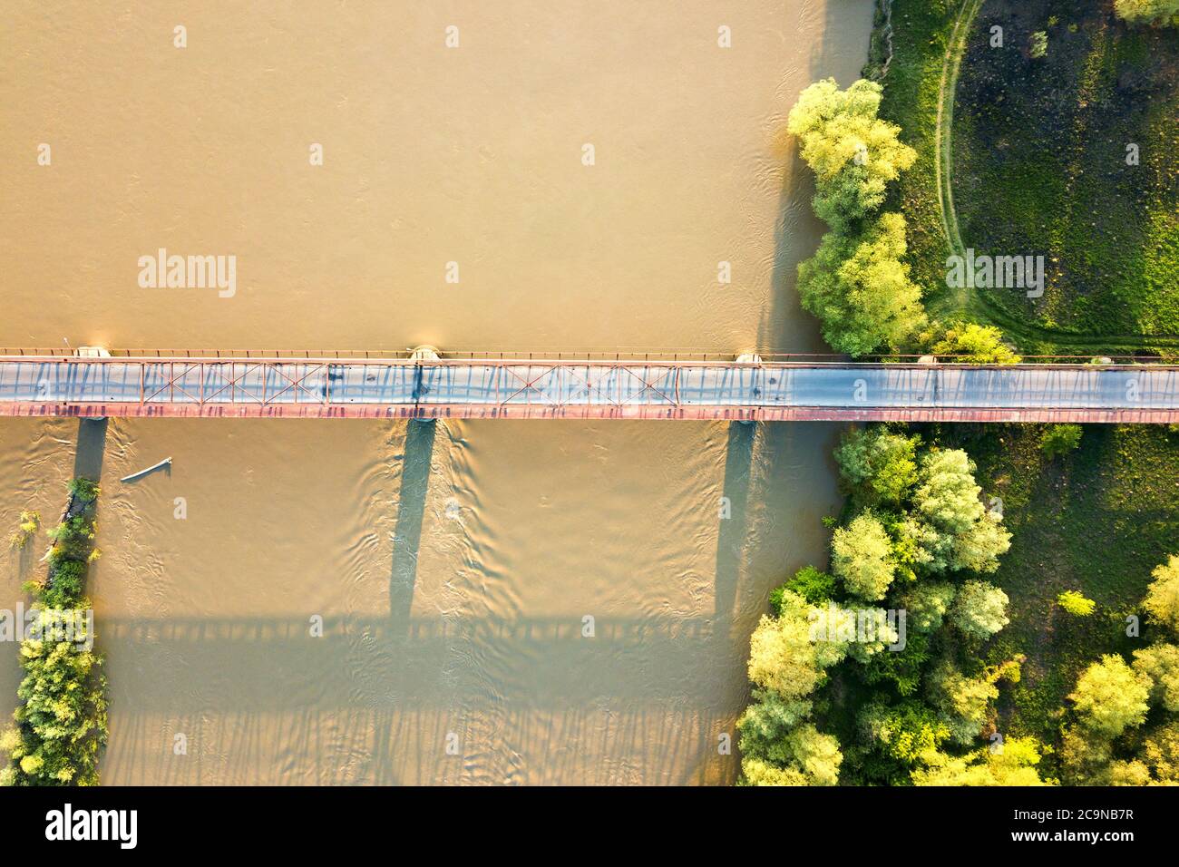 Aerial view of a narrow road bridge stretching over muddy wide river in ...