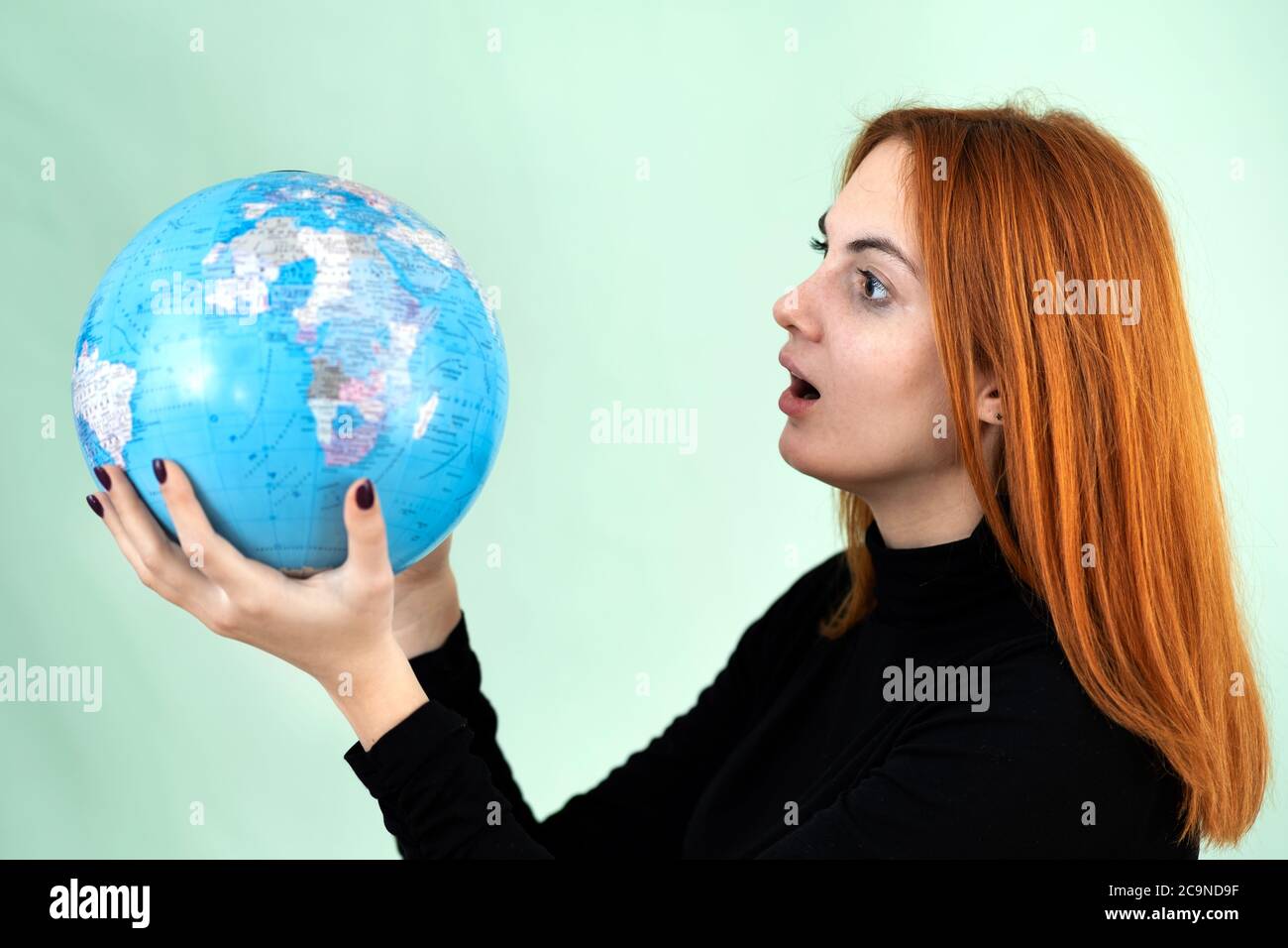 Portrait of a sad worried young woman holding geographic globe of the ...
