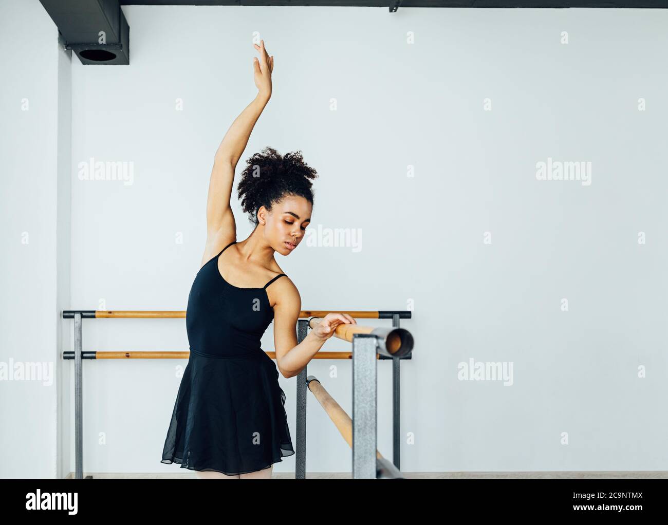 Young beautiful ballerina practicing ballet moves at barre in small ...