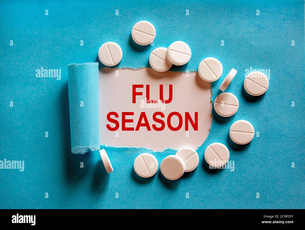 The text 'flu season' appearing behind torn blue paper. White pills ...