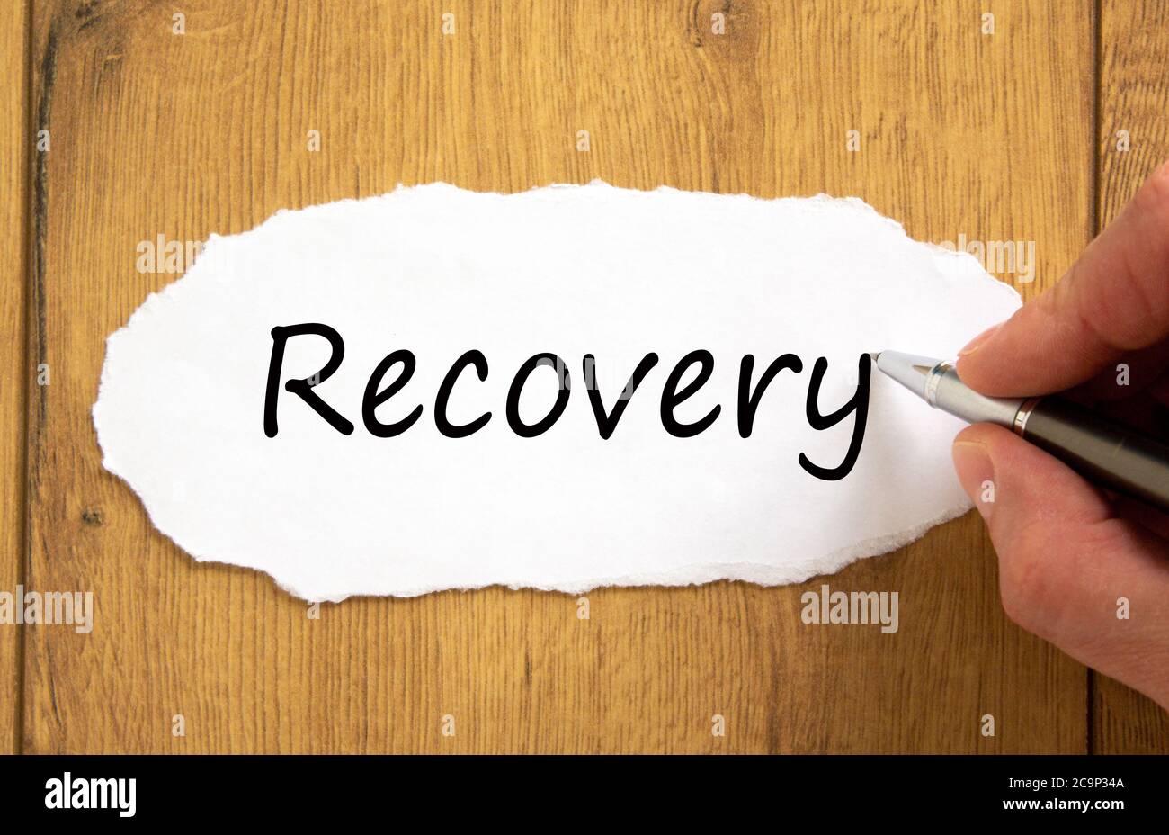 Male hand writing 'recovery' on white paper on wooden table. Business ...