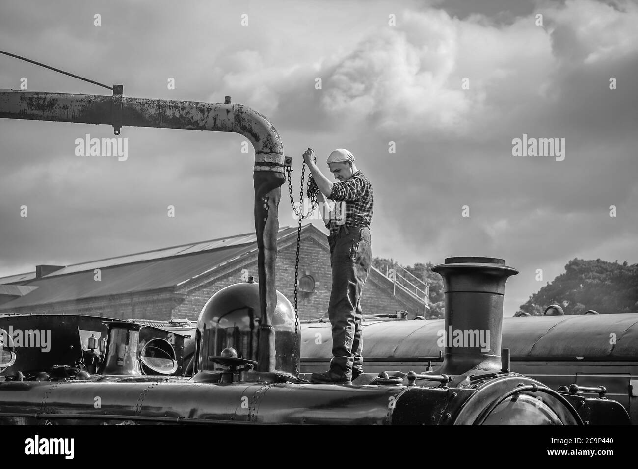Steam train crew fireman filling water tank of vintage steam locomotive ...