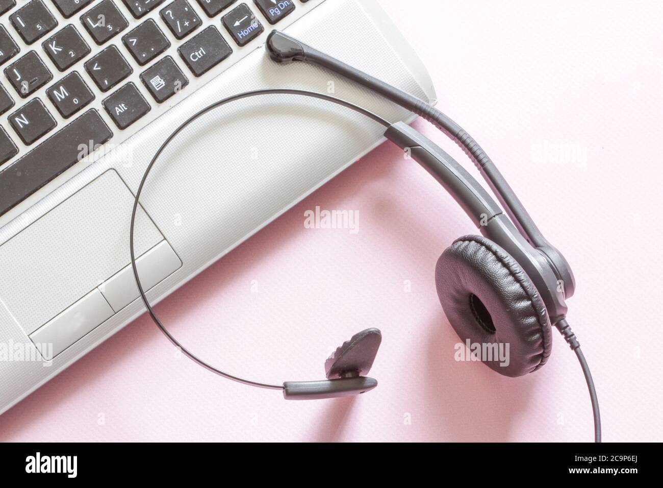 Office desk with headset and keyboard on the pink background ...
