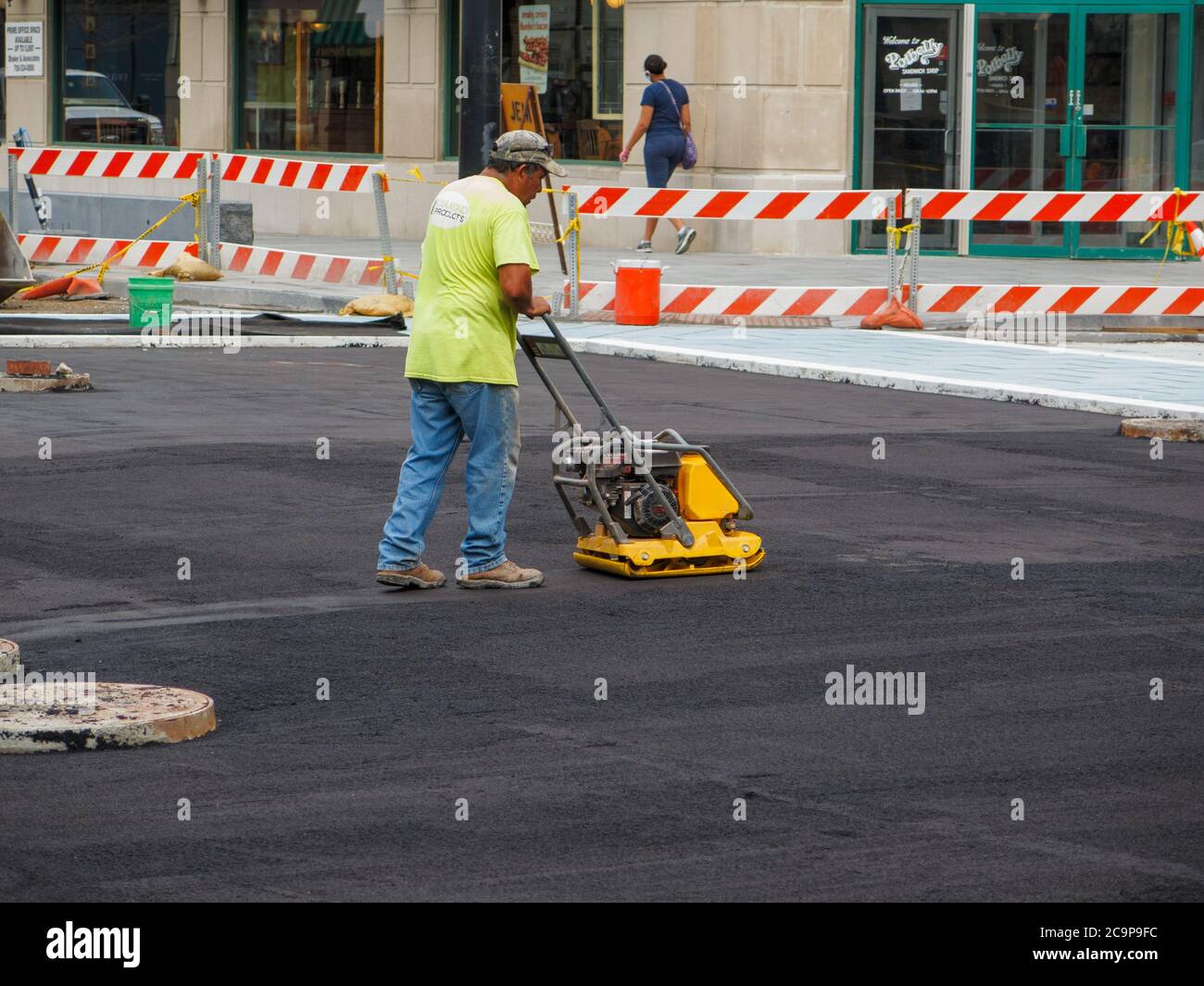 Construction worker using power tamper to tamp freshly laid asphalt ...