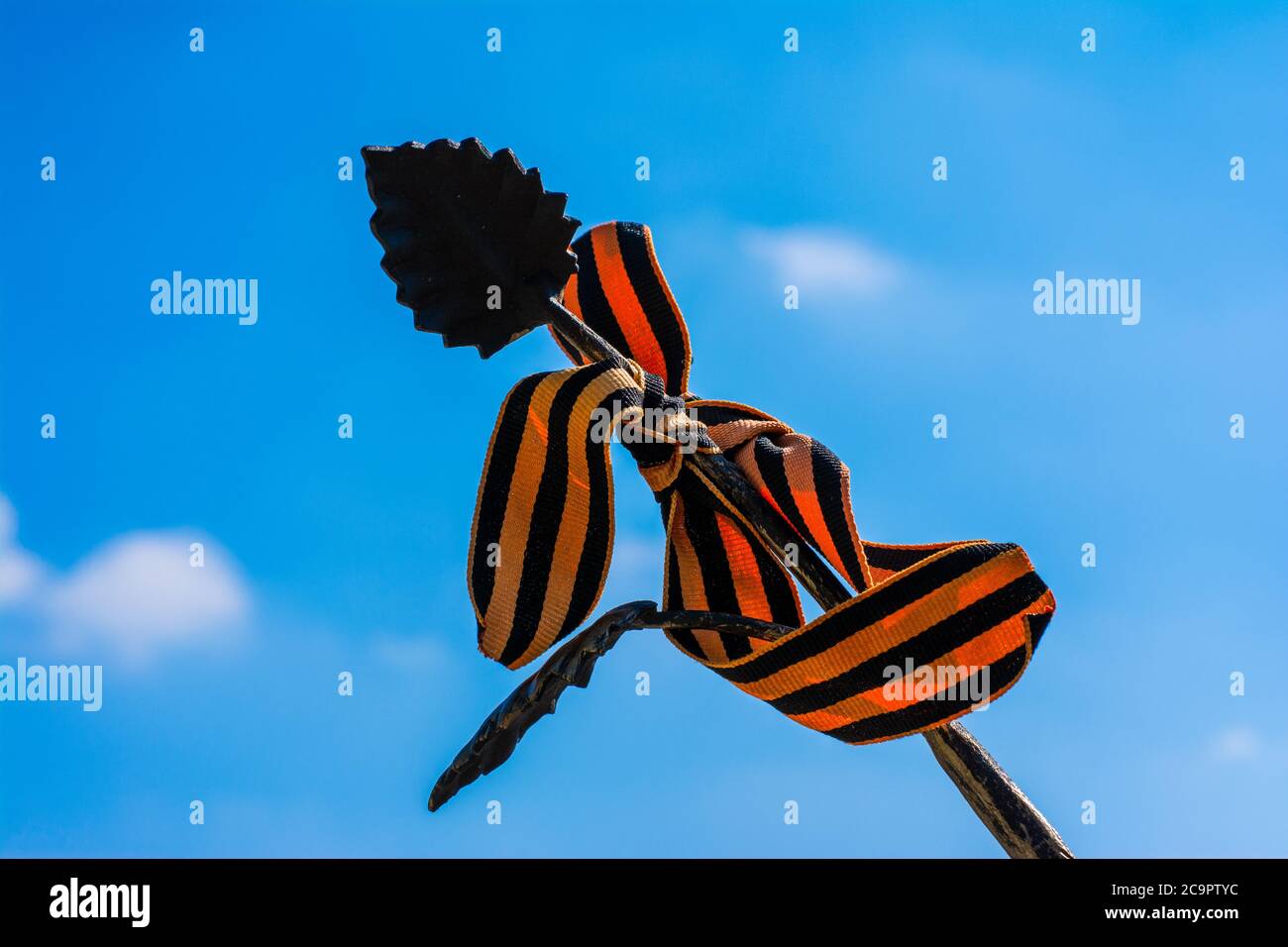 Forged iron leaf wrapped St. George ribbon on a background of blue sky ...