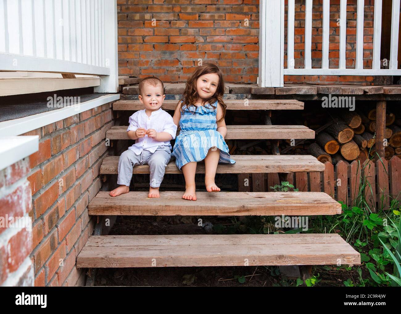 Cute little brother and sister sitting on wooden staircase near porch ...