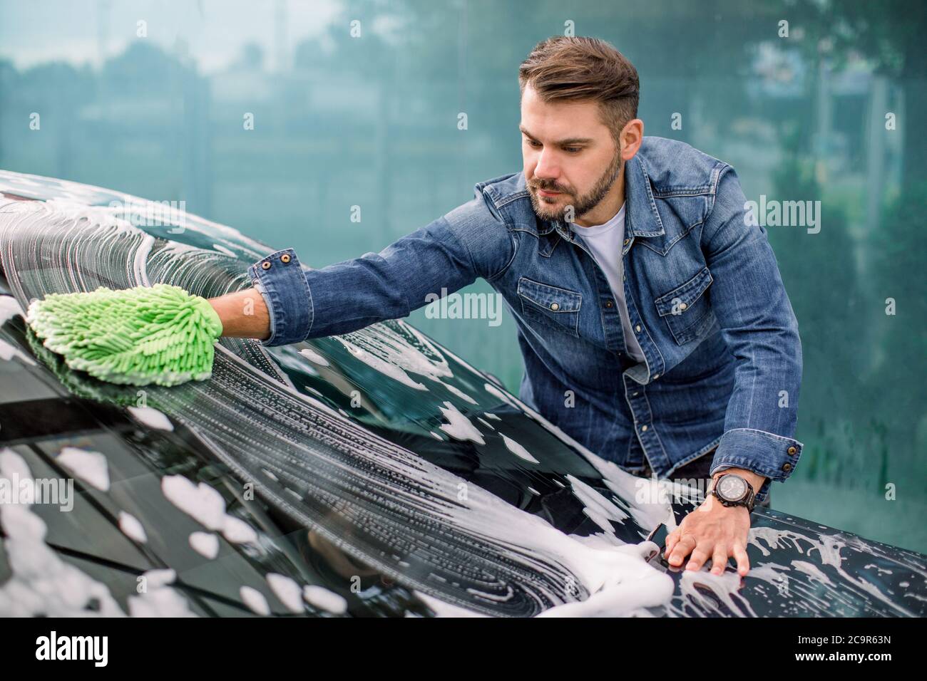 Handsome young Caucasian man cleaning his car windshield with green ...
