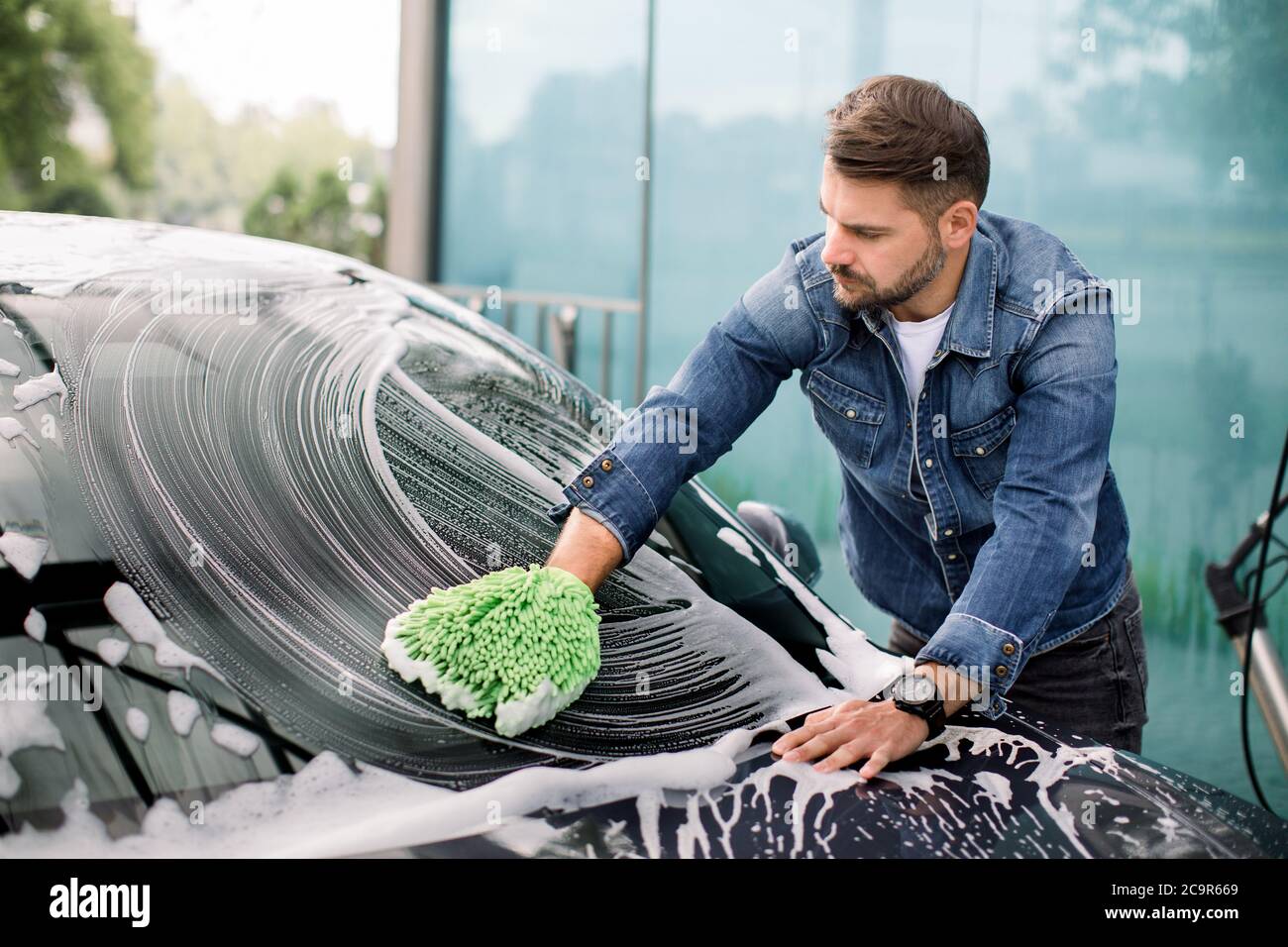 Handsome young Caucasian man cleaning his car windshield with green ...