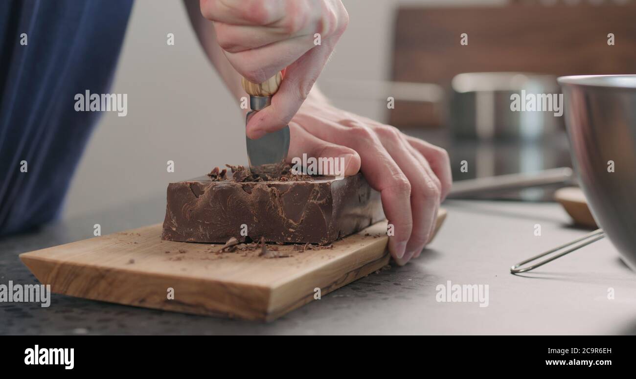 man hands breaking big dark chocolate block with knife on wood board ...