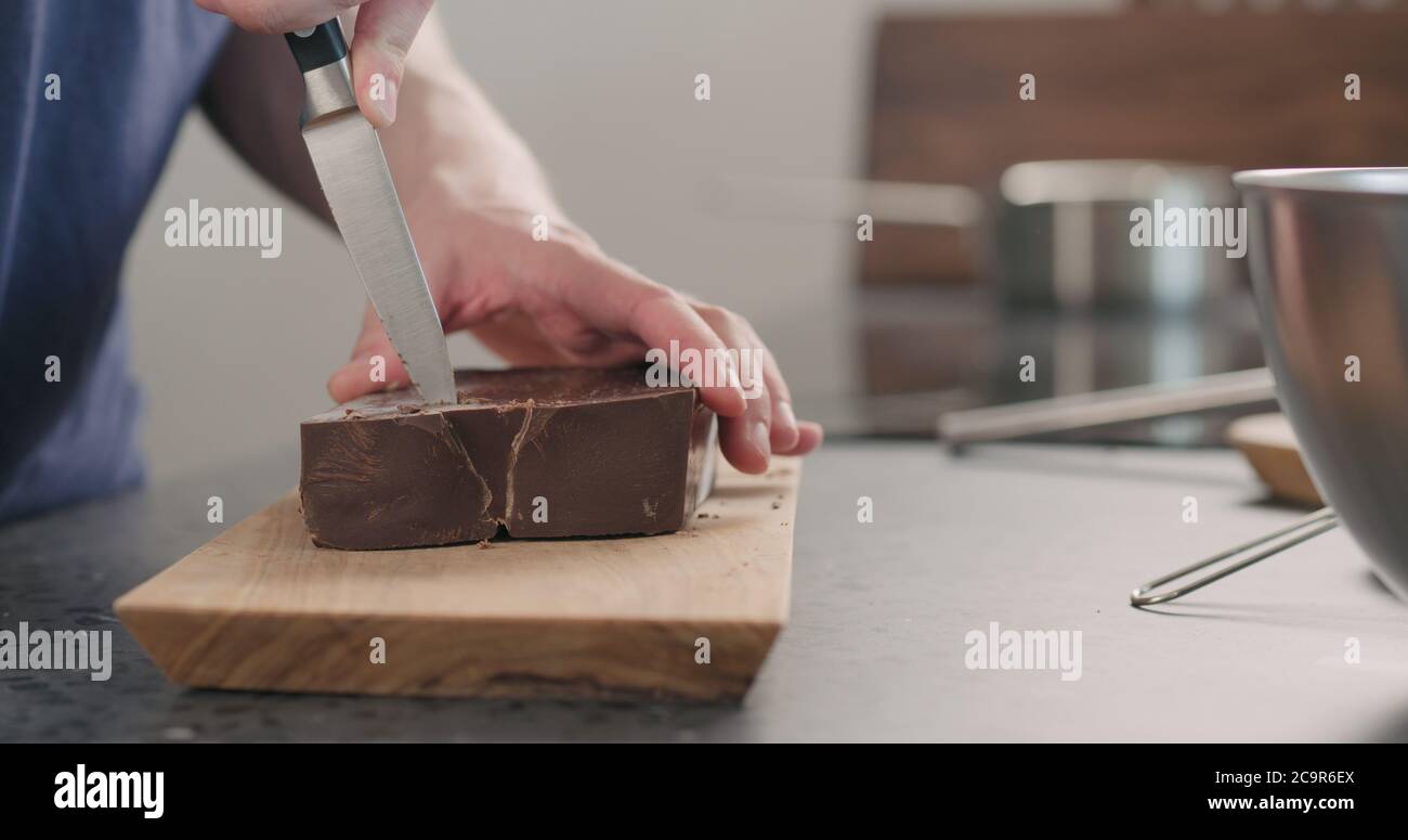 man hands breaking big dark chocolate block with knife on wood board ...