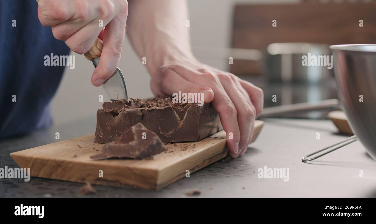 man hands breaking big dark chocolate block with knife on wood board ...