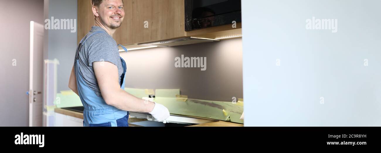 Happy man in work clothes sets hob in kitchen Stock Photo - Alamy