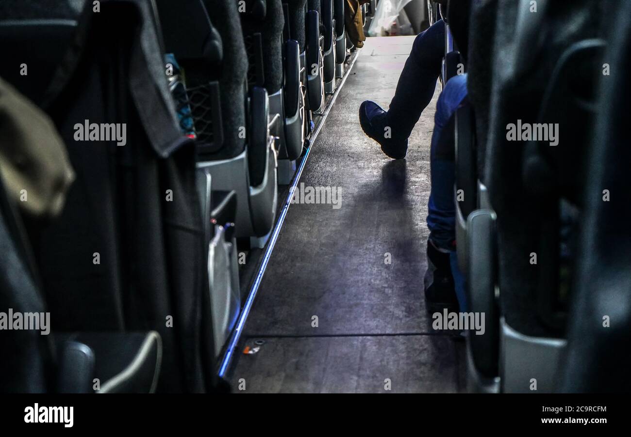 Coach bus seats seen from back row, one passenger has his foot in aisle ...