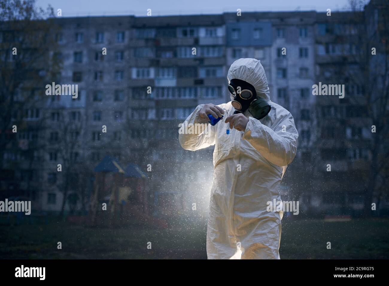 Scientist wearing a coverall and a gas mask, holding glass flasks with ...